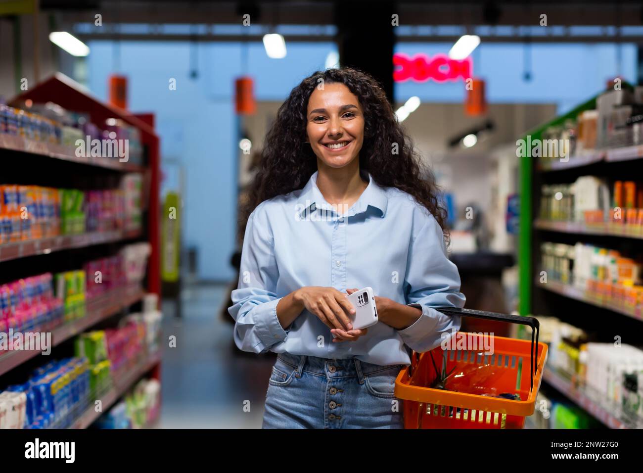 Shopping in a supermarket. A young Hispanic woman walks between rows of ...