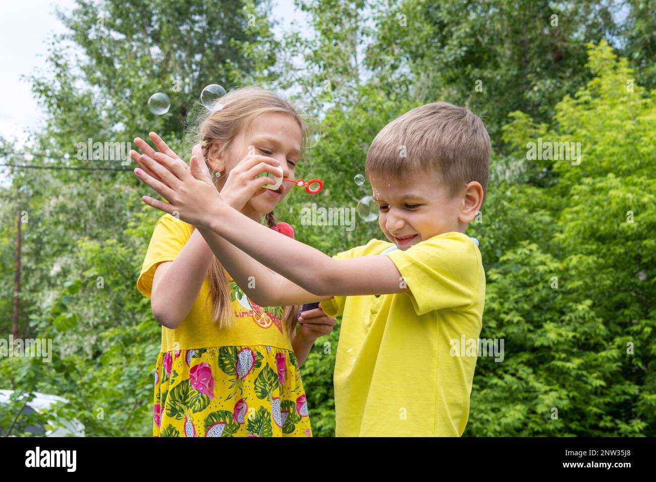 Happy kids boy and girl have fun in the park blowing rainbow bubbles ...