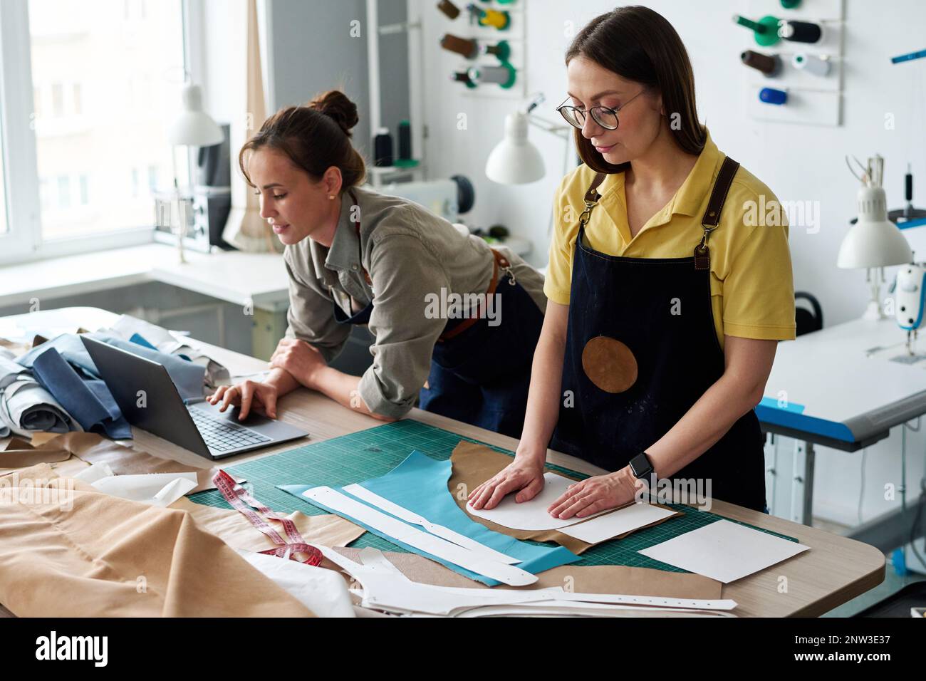 Mature female tailor putting pattern on piece of leather against young ...