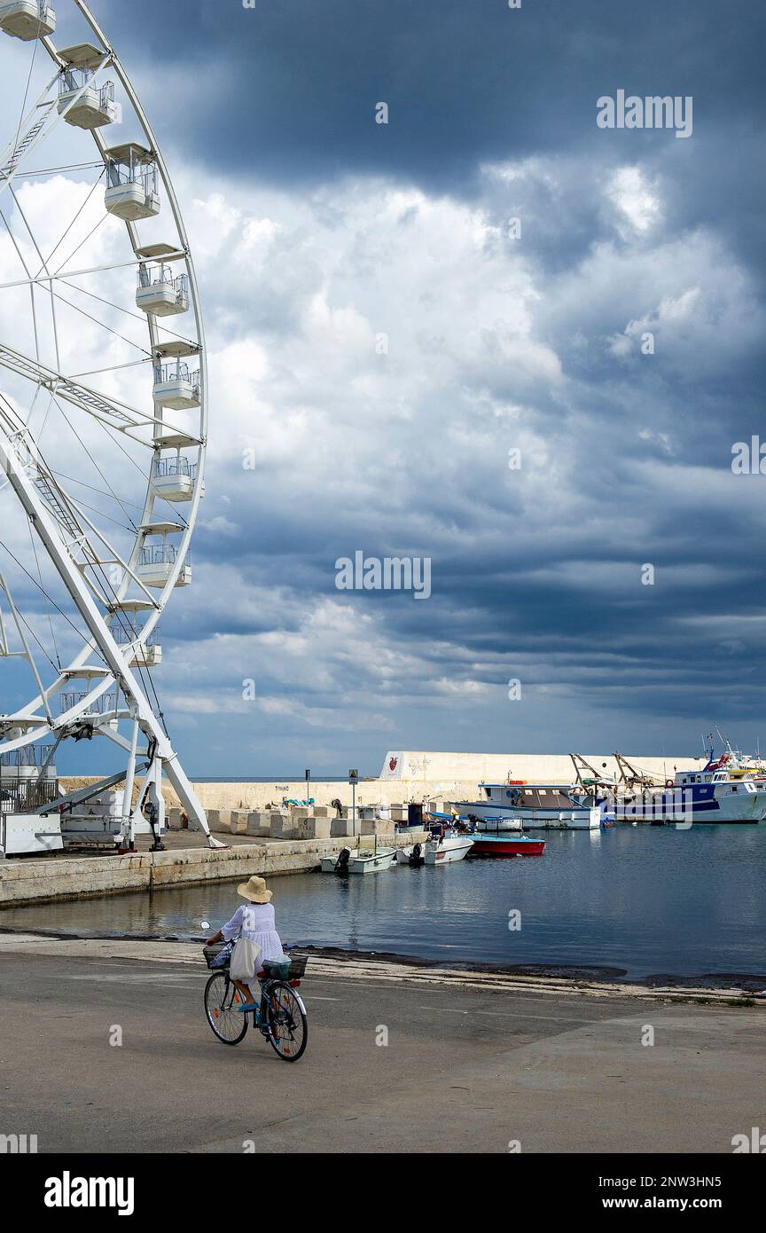 Woman riding a bicycle by the small port in Campomarino, dominated by a ...