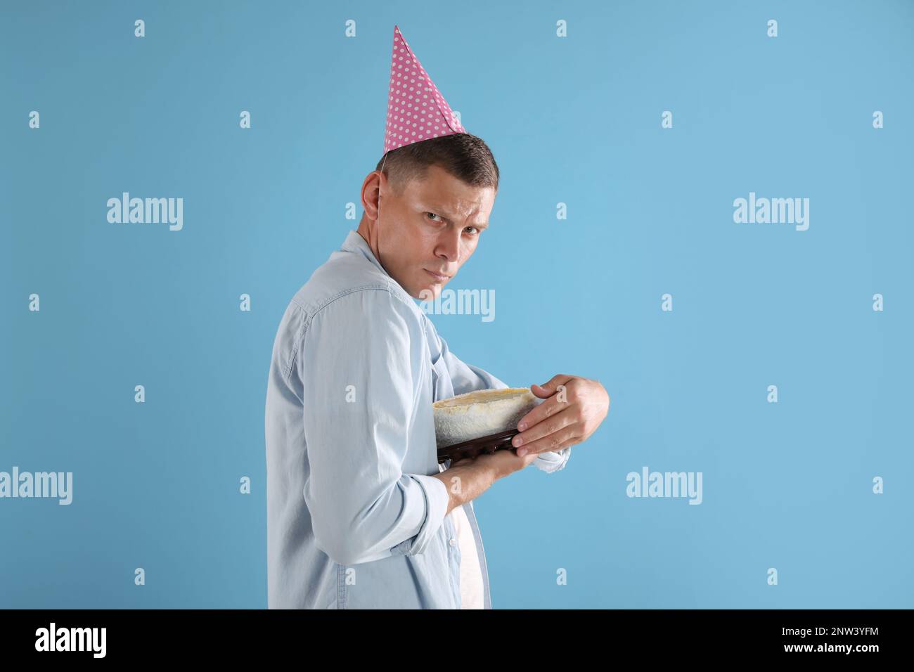 Greedy man with party hat hiding birthday cake on turquoise background ...