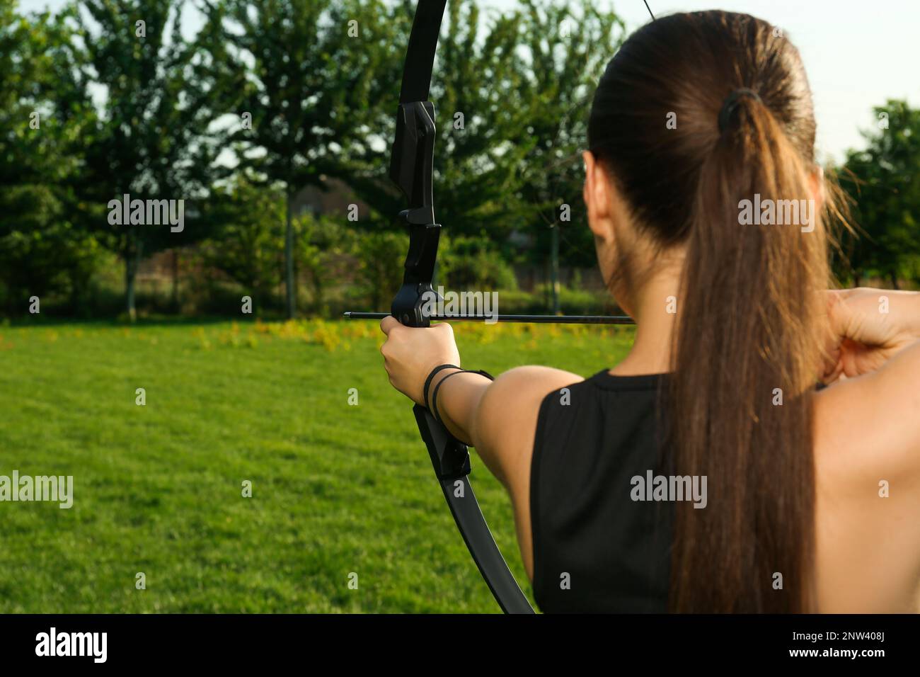 Woman with bow and arrow practicing archery in park, back view Stock ...