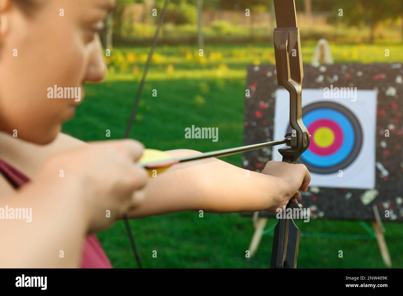 Woman with bow and arrow aiming at archery target in park, closeup ...