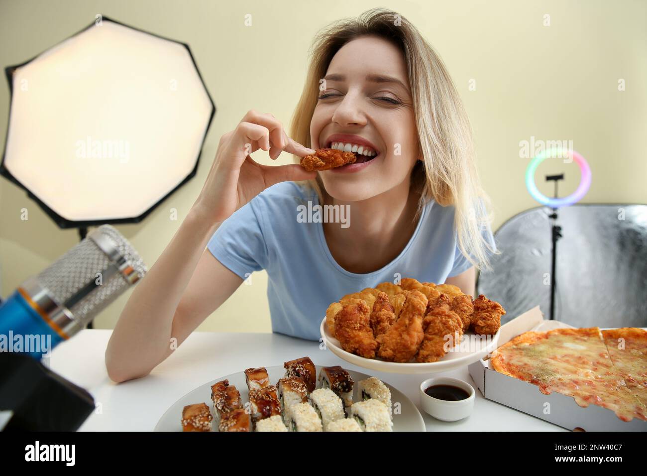 Food blogger eating in front of microphone at table against light ...
