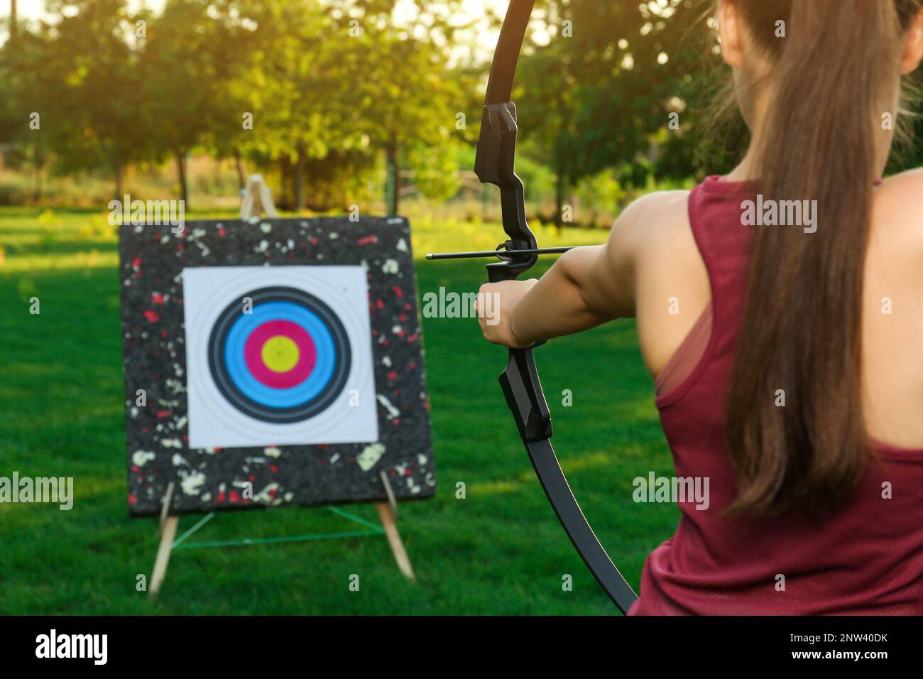 Woman with bow and arrow aiming at archery target in park, back view ...