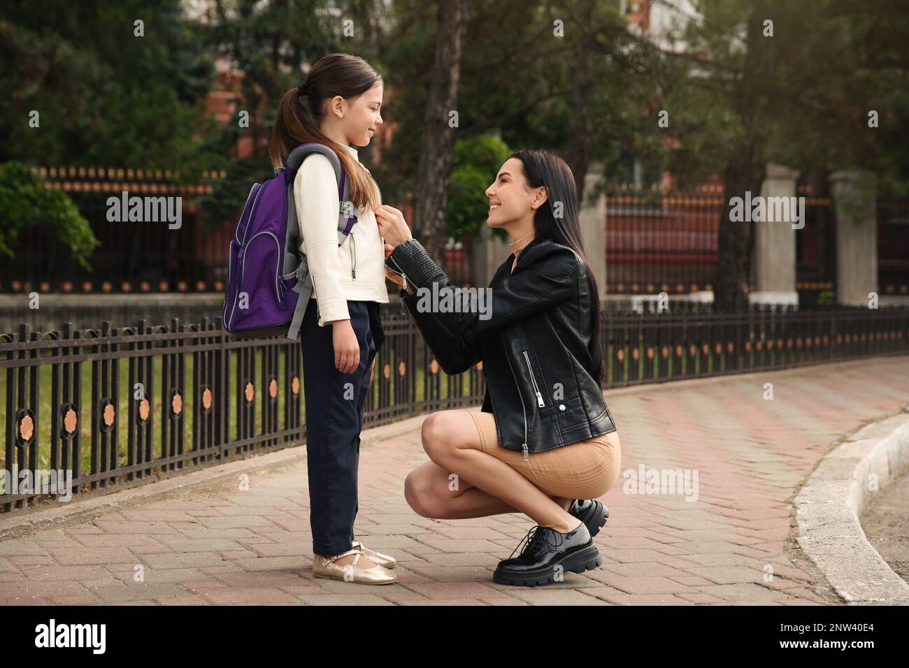 Happy mother helping her little daughter to zipper jacket before school ...