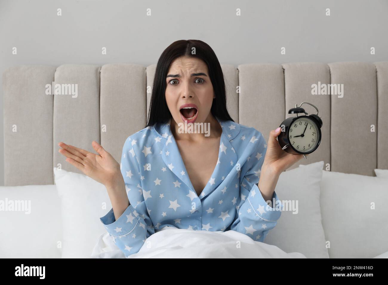 Emotional overslept woman with alarm clock in bed. Being late concept ...