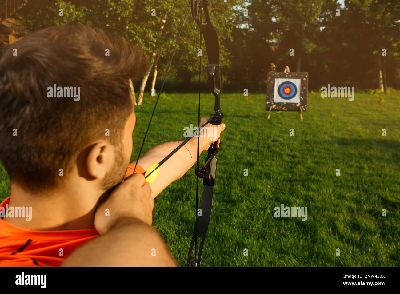 Man with bow and arrow aiming at archery target in park, back view ...