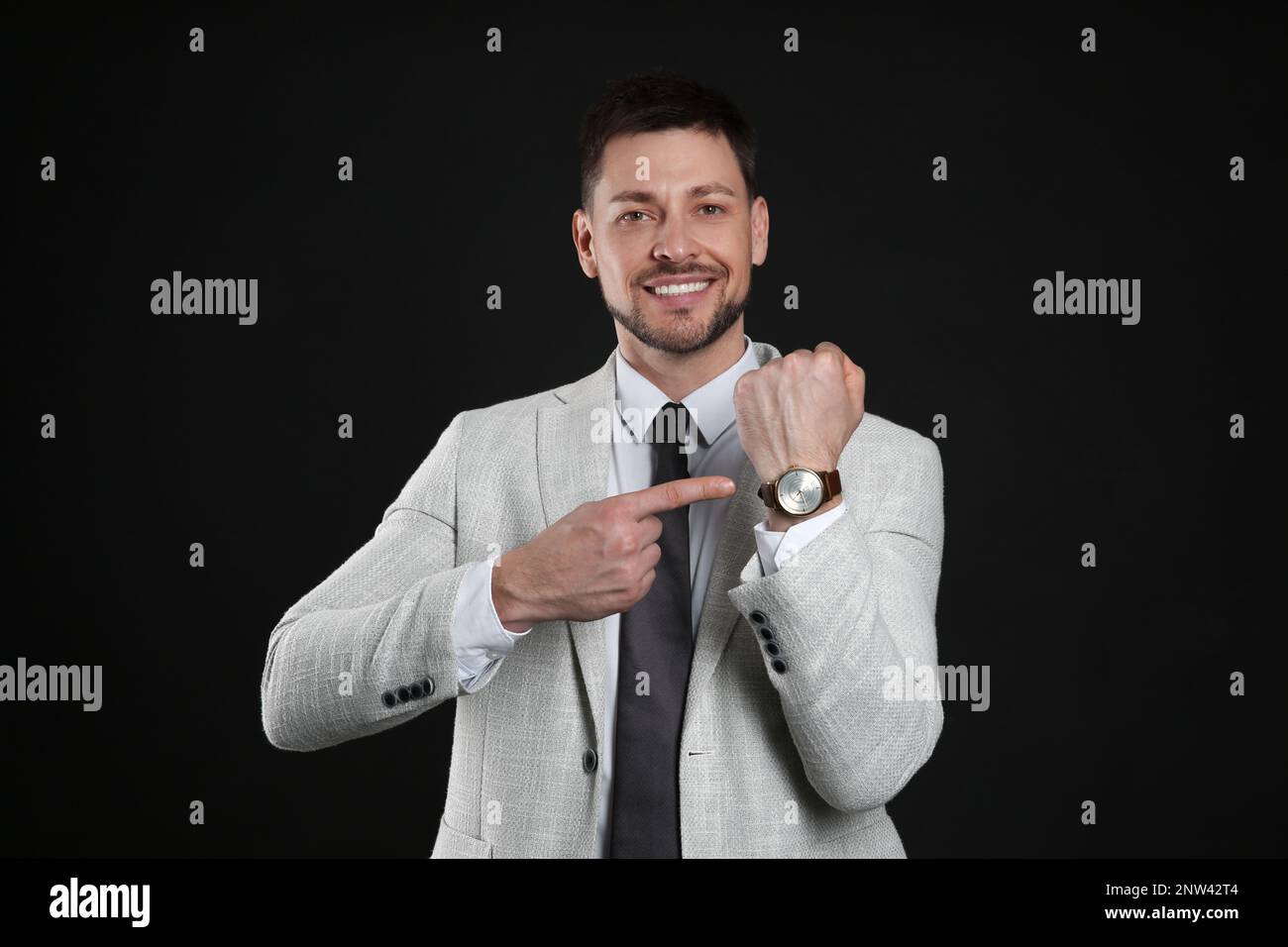 Happy businessman pointing on wristwatch against black background. Time ...
