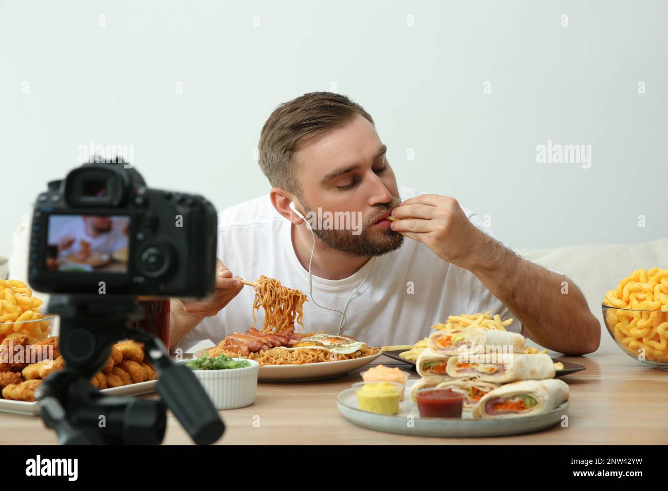 Food blogger recording eating show on camera against light background ...
