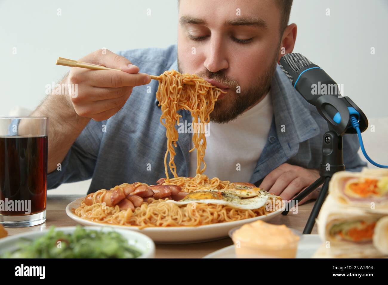 Food blogger eating in front of microphone at table against light ...