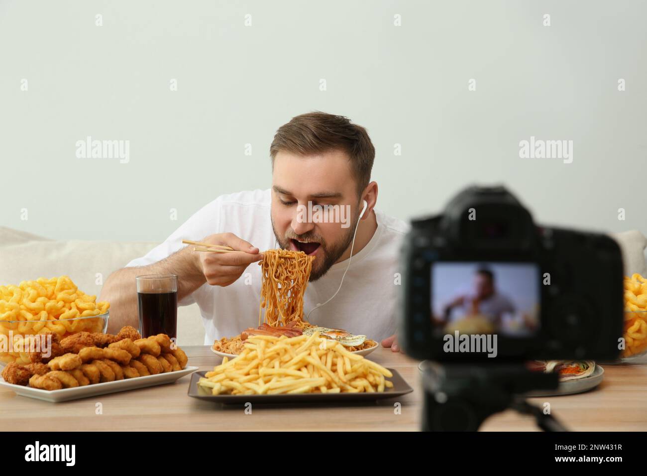 Food blogger recording eating show on camera against light background ...