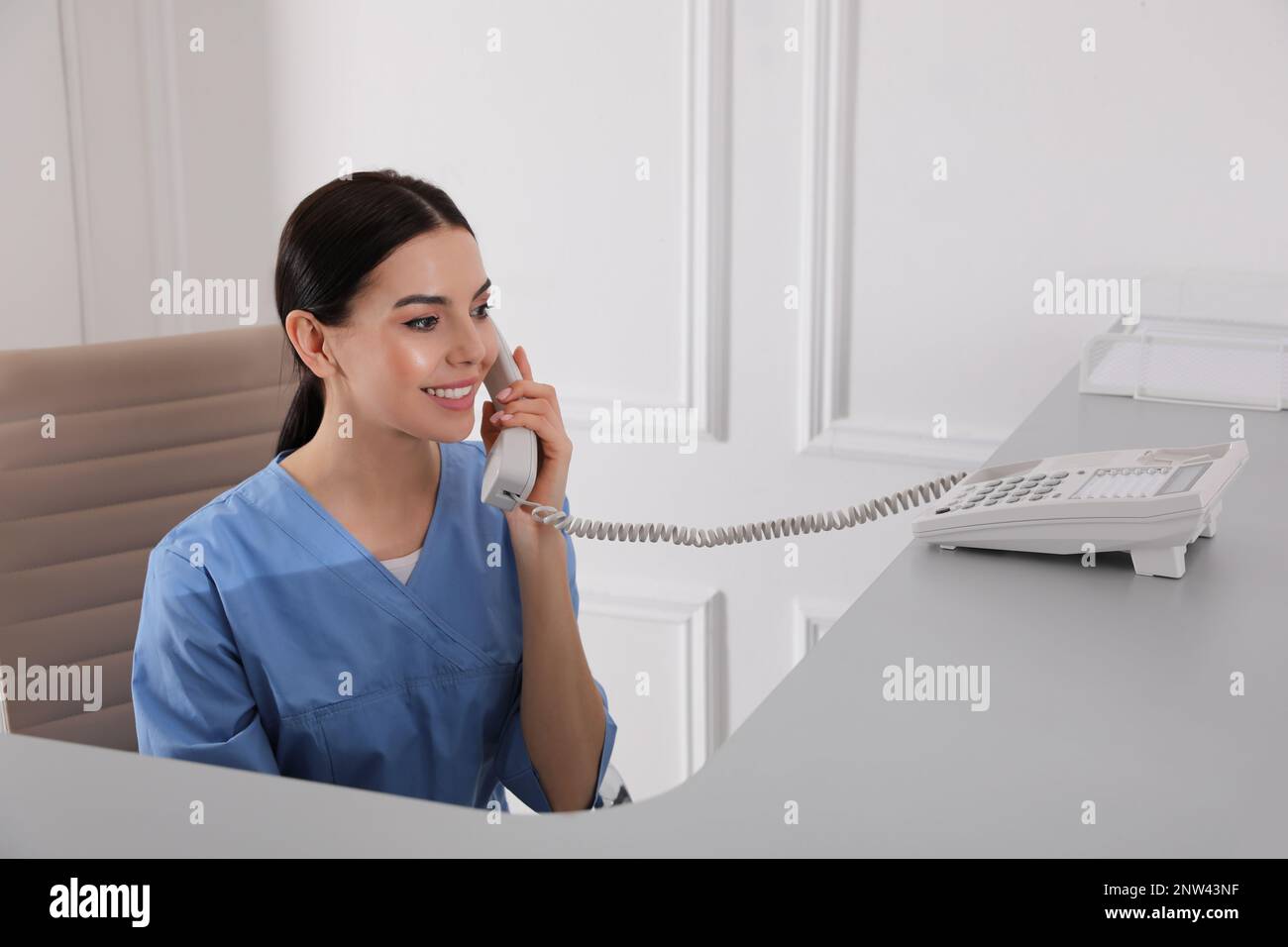 Receptionist talking on phone at countertop in hospital Stock Photo - Alamy