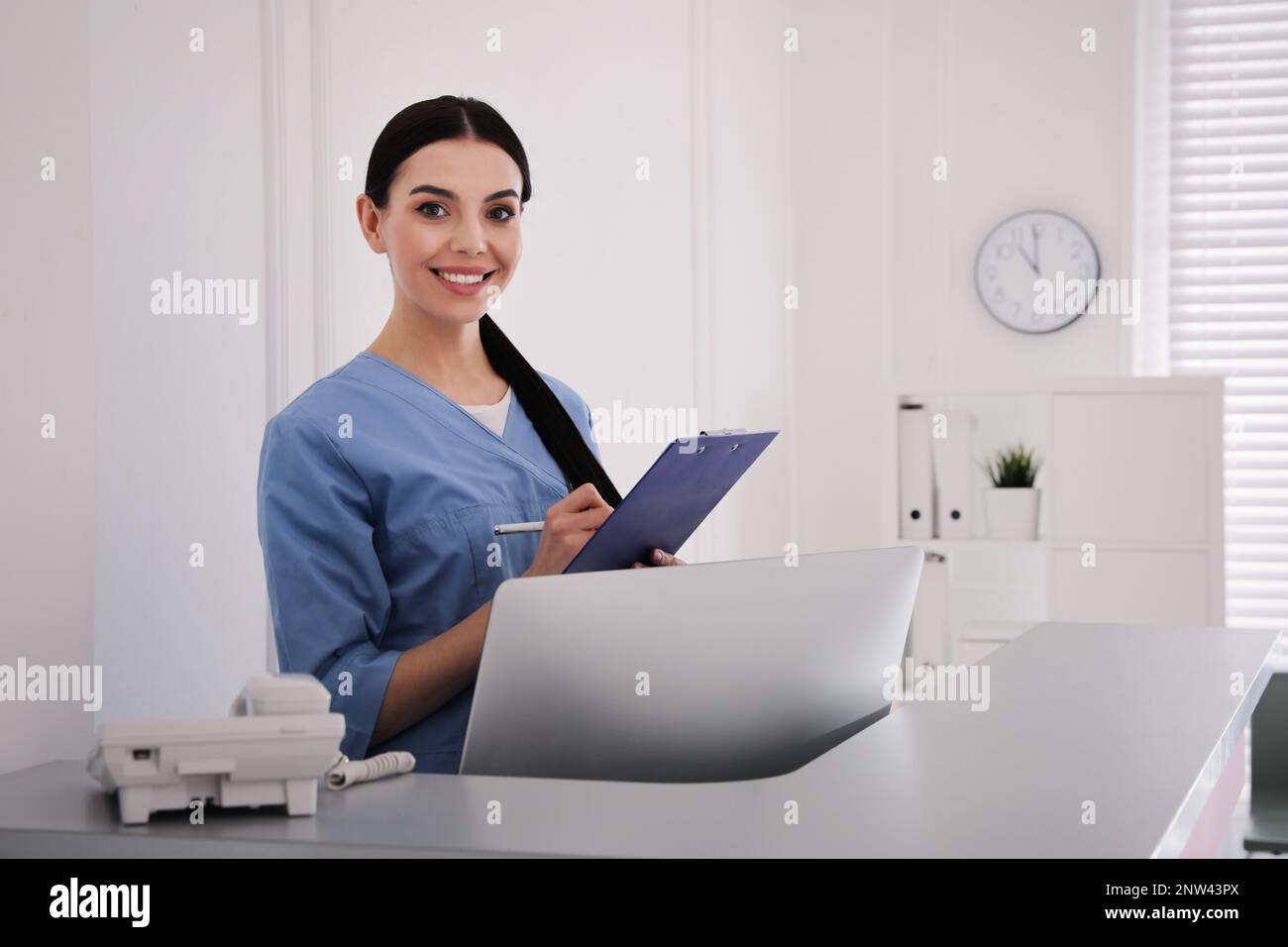 Receptionist with clipboard at countertop in hospital Stock Photo - Alamy