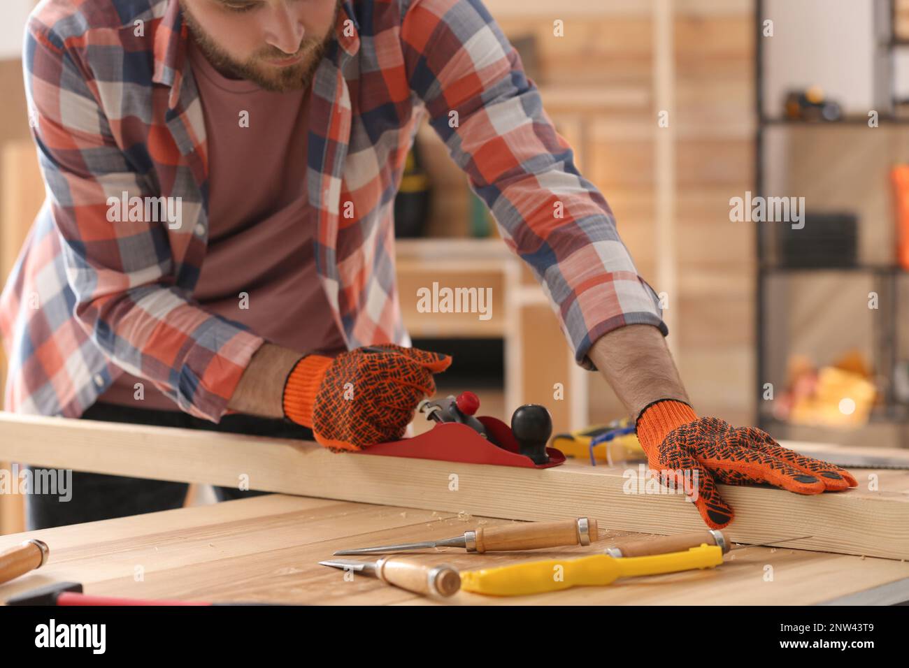 Carpenter shaping wooden bar with hand plane at table in workshop ...