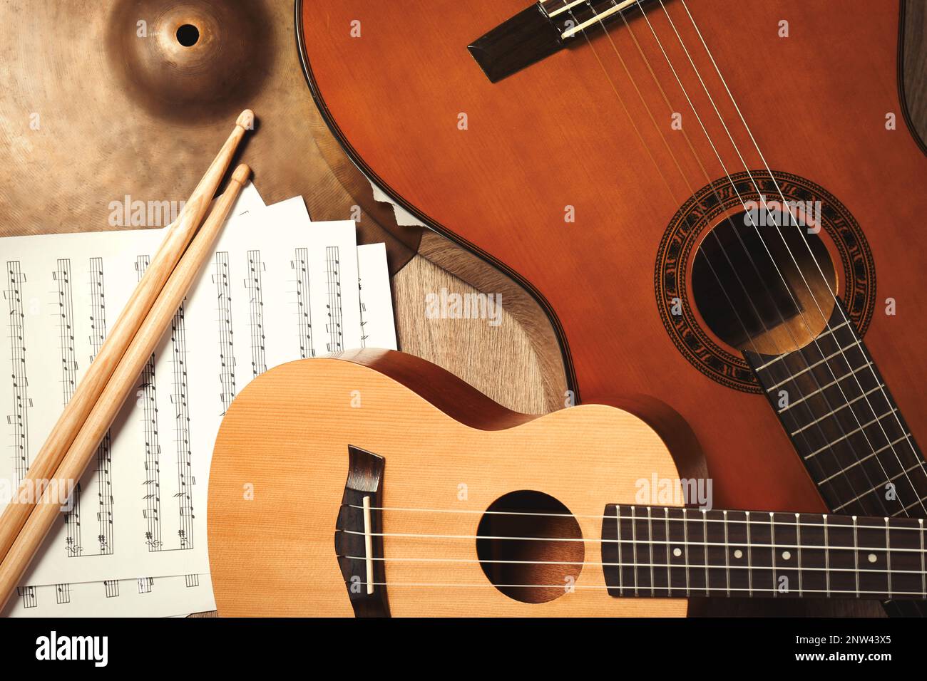 Ukulele, acoustic guitar, drumsticks, cymbal and note sheets on wooden ...