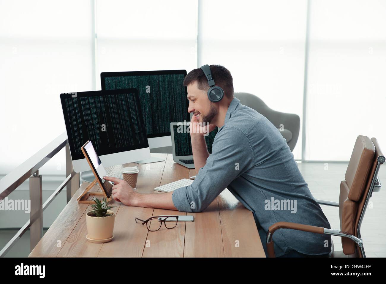 Happy programmer with headphones working at desk in office Stock Photo ...
