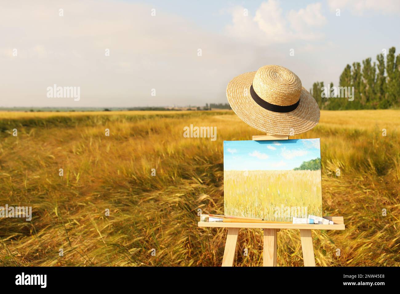 Wooden easel with beautiful picture, painting equipment and hat in ...