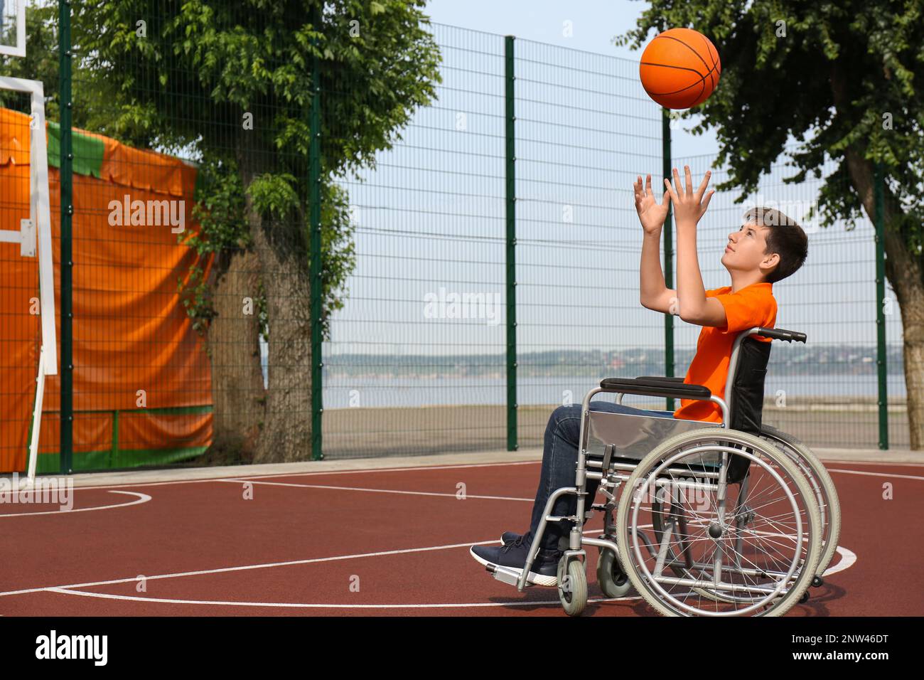 Disabled teenage boy in wheelchair playing basketball on outdoor court ...