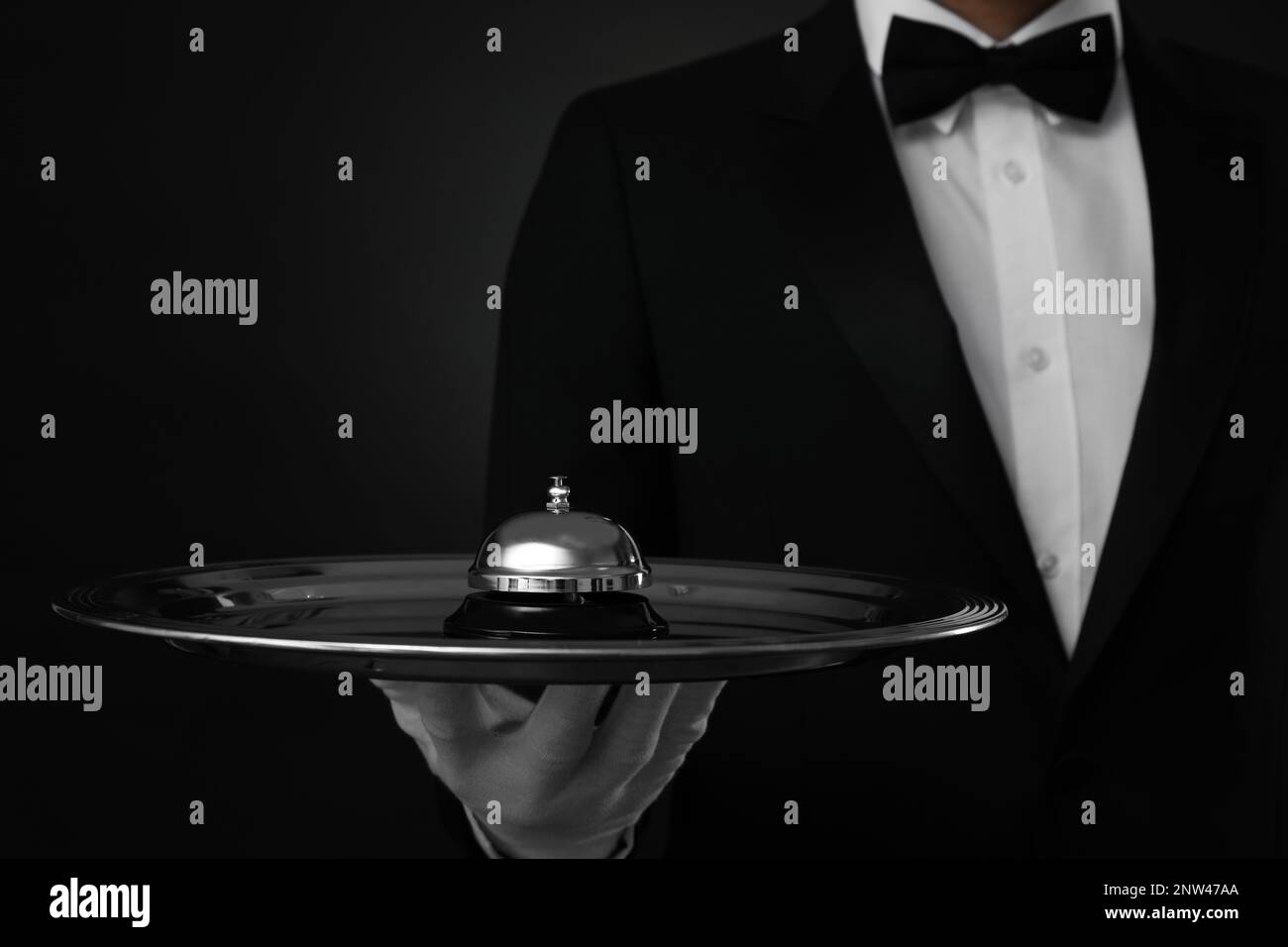 Butler holding metal tray with service bell on black background ...