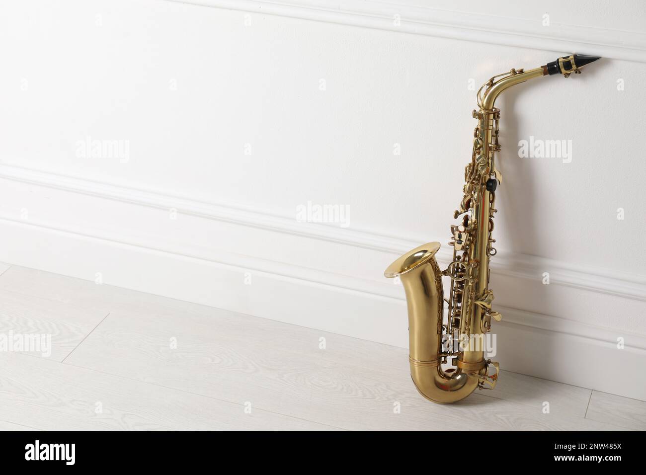 Beautiful saxophone on floor near white wall indoors, space for text ...