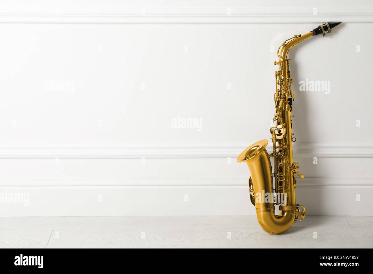 Beautiful saxophone on floor near white wall indoors, space for text ...