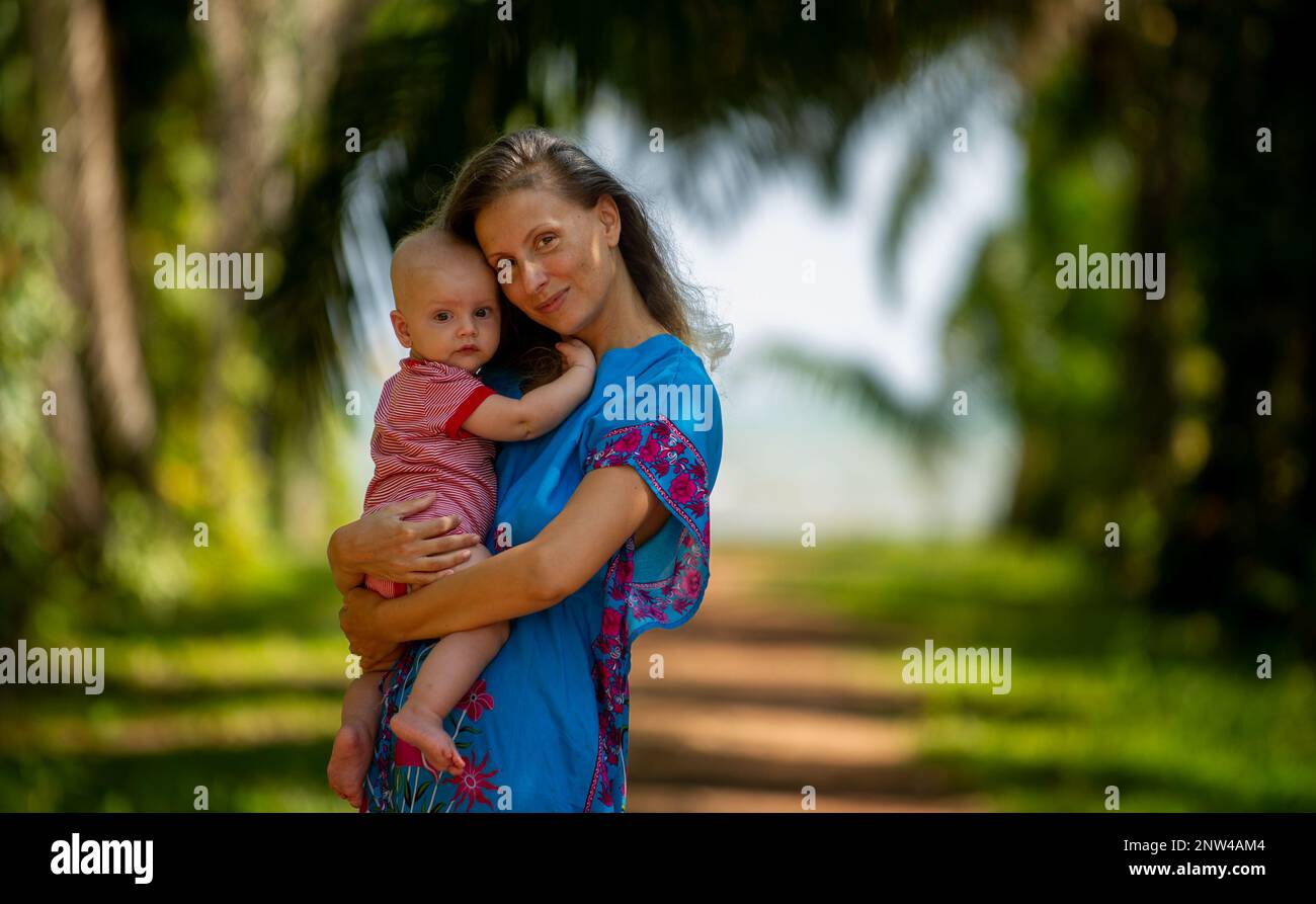 Mother with adorable baby on holiday in Thailand walking through palm ...