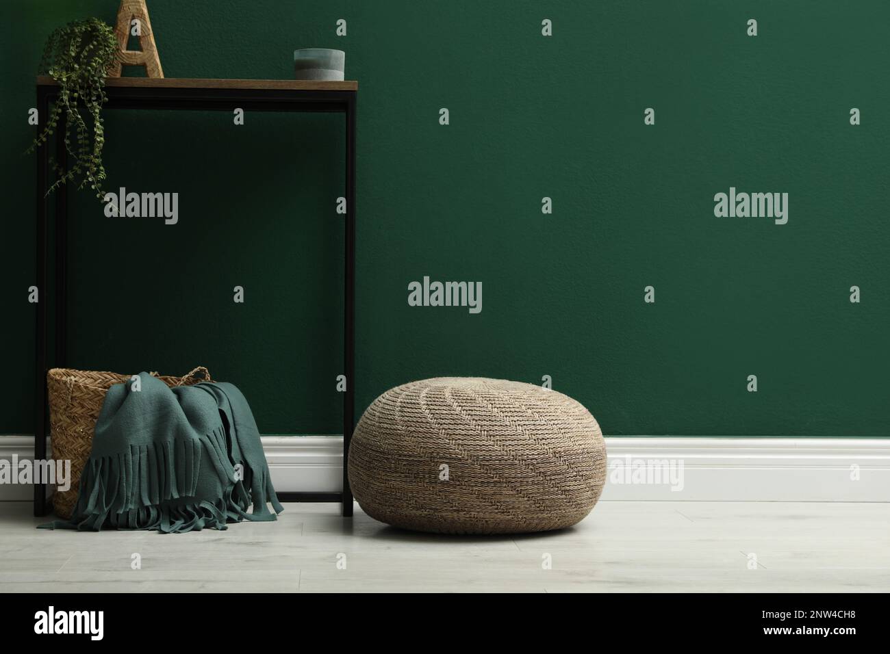 Stylish knitted pouf and table near green wall indoors, space for text ...