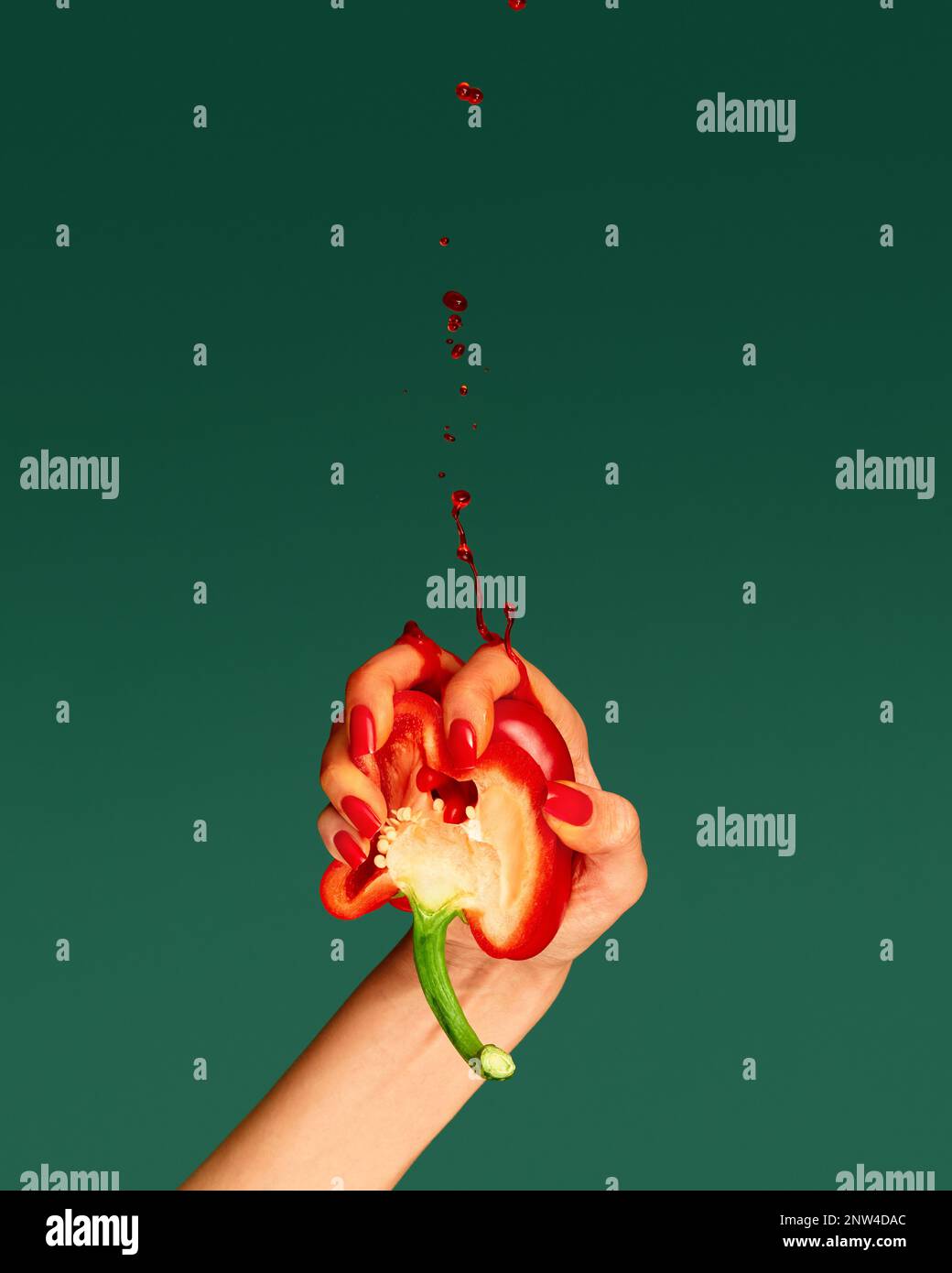 Red pepper juice. Female hand squeeze pepper and drops flying up over ...