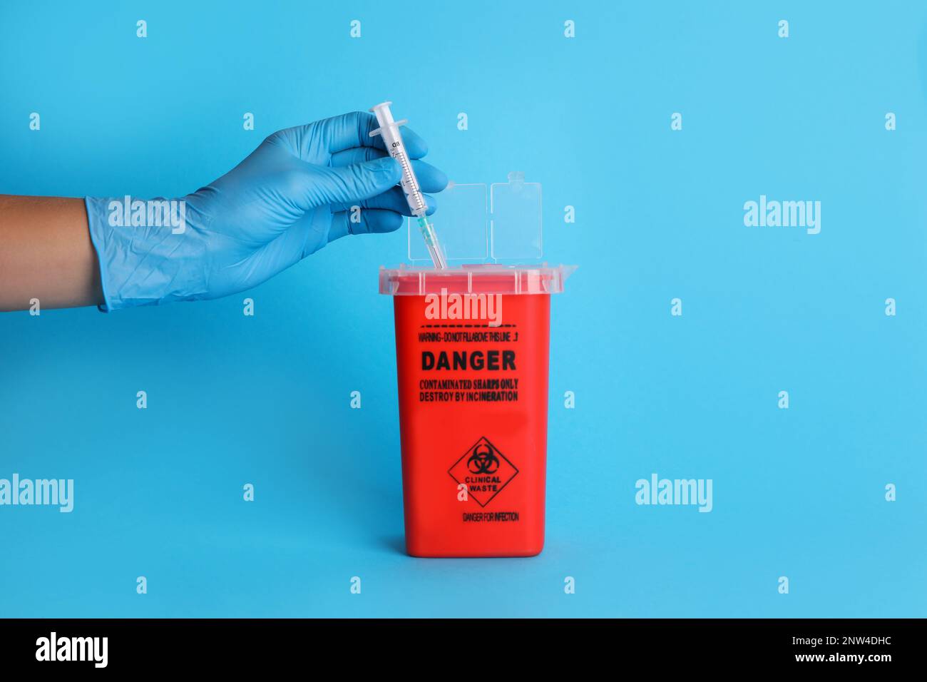 Doctor throwing used syringe into sharps container on light blue ...