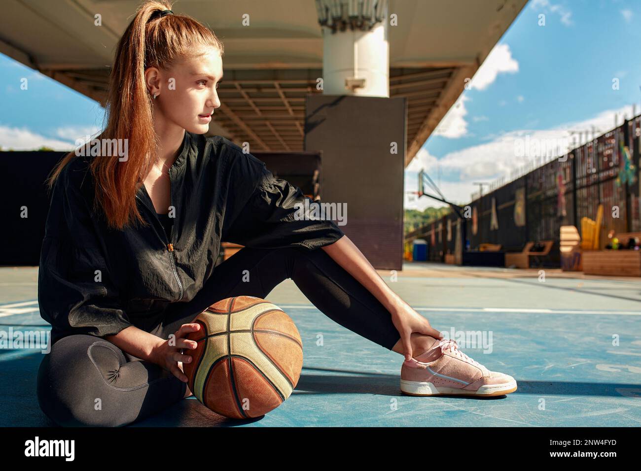 Beautiful woman in sports uniform with a basketball ball, sitting on ...