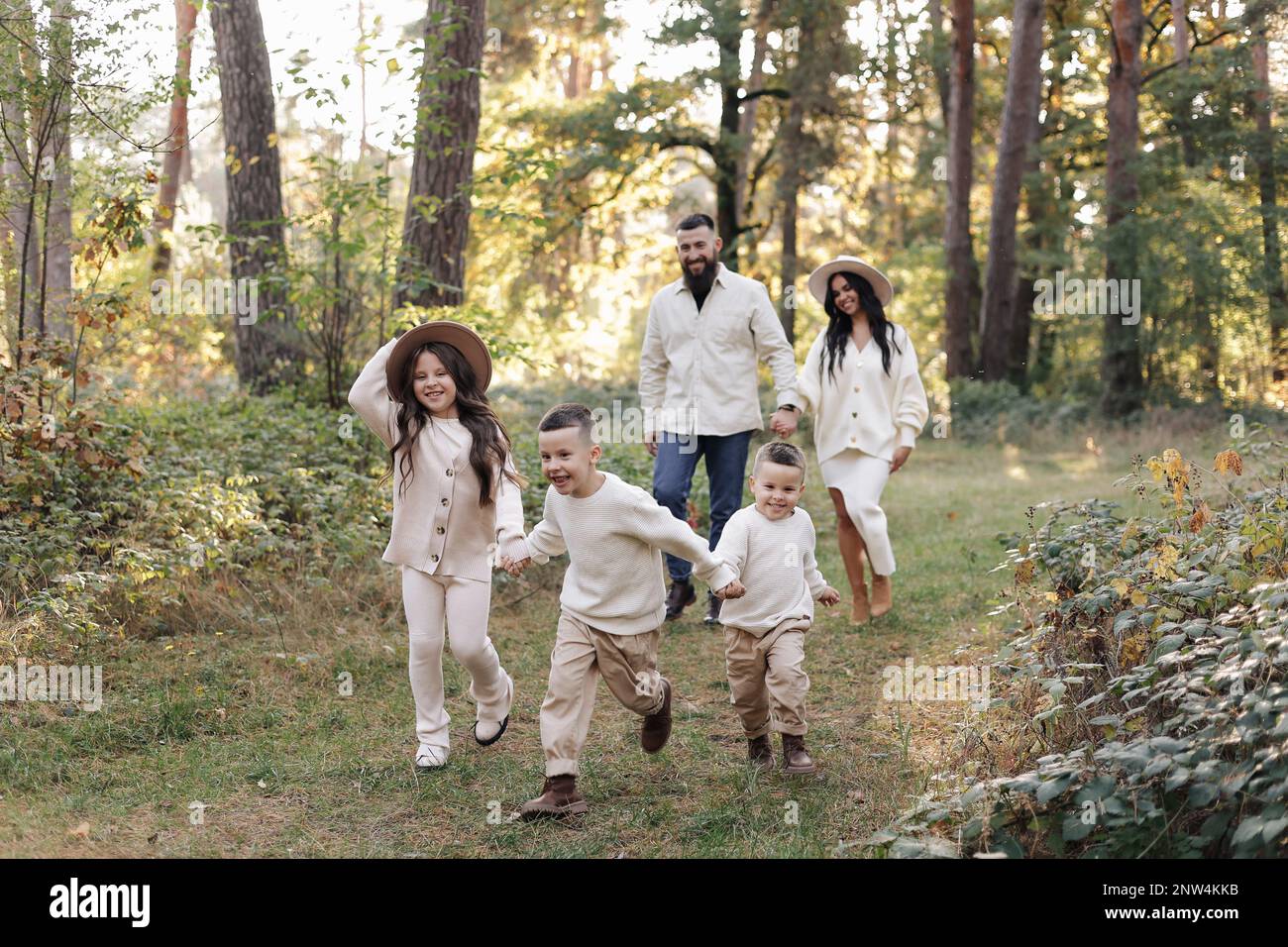 Young mother, father with daughter and sons are walking, having fun in autumn forest. Family ...