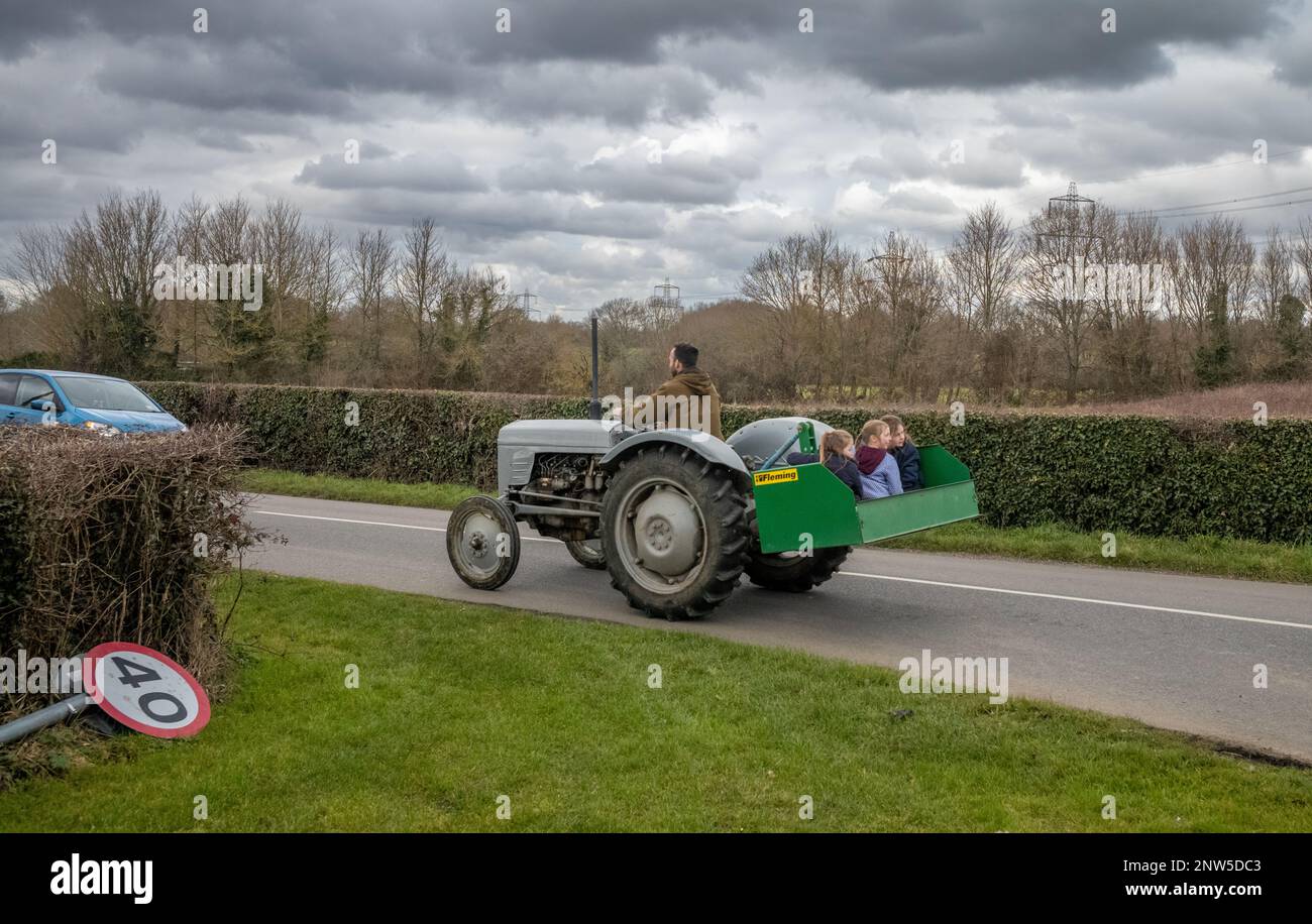 A man drives a vintage tractor down a country lane with three young ...