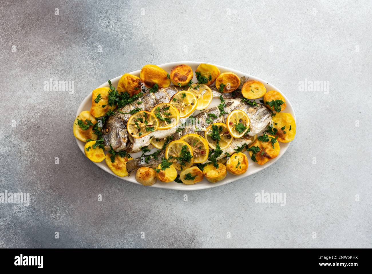 Oven-baked Dorada fish with potatoes and lemon slices, sprinkled with ...