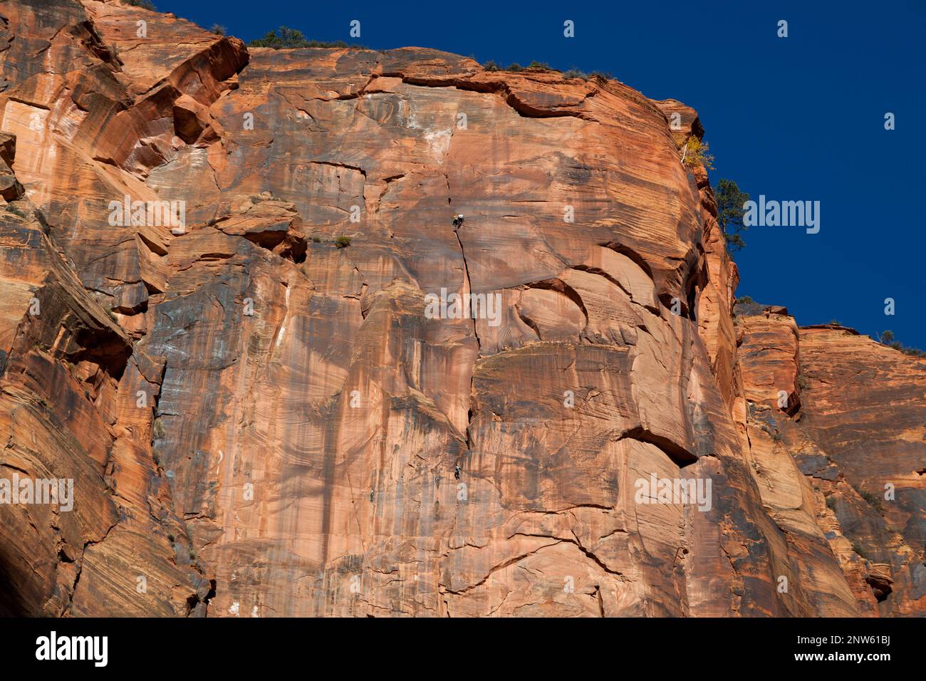 Three adventurous people climb up a giant crack in the tall cliff face ...