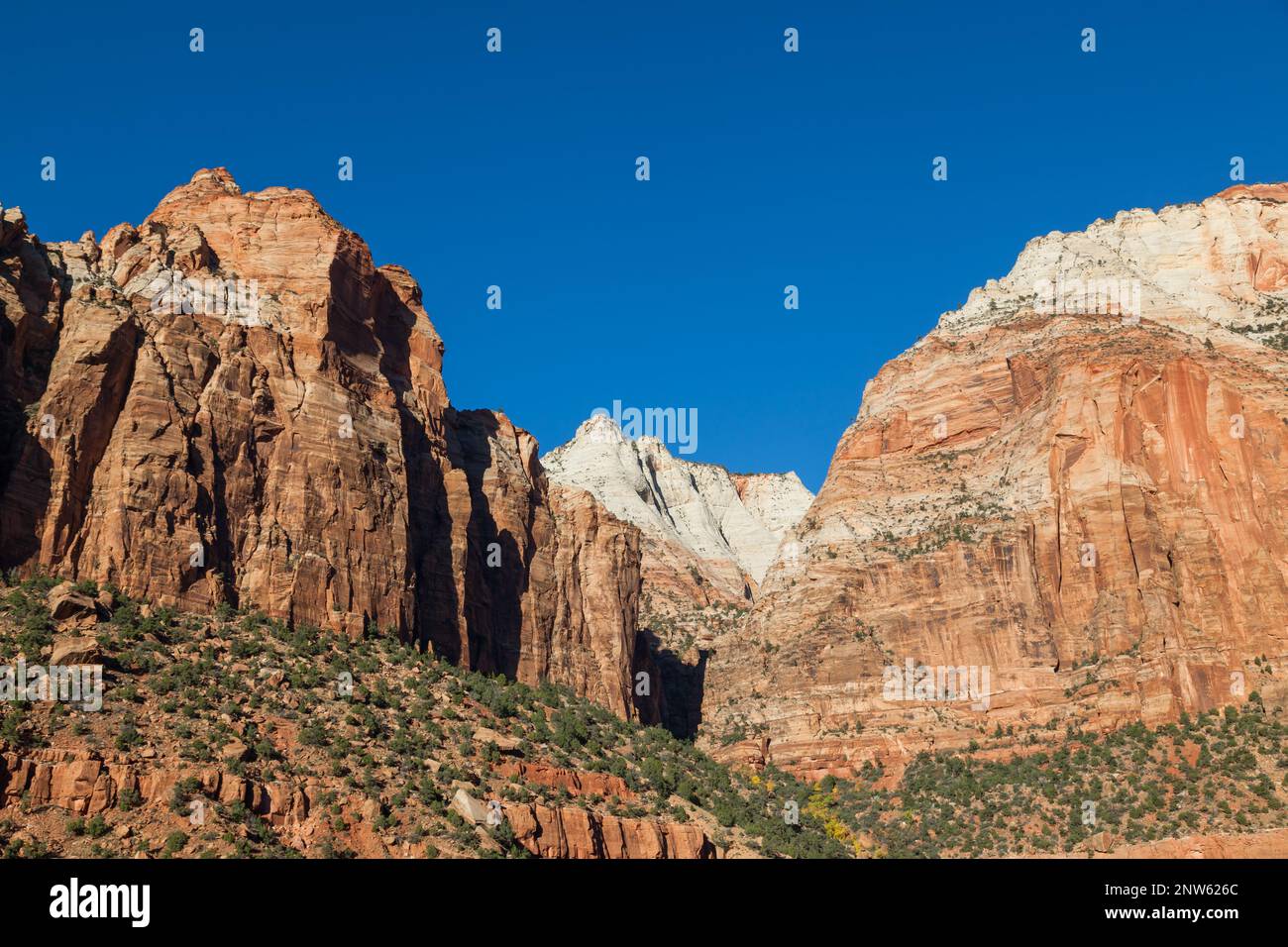 Tall rock cliffs rise up from the desert floor and into the clear blue ...