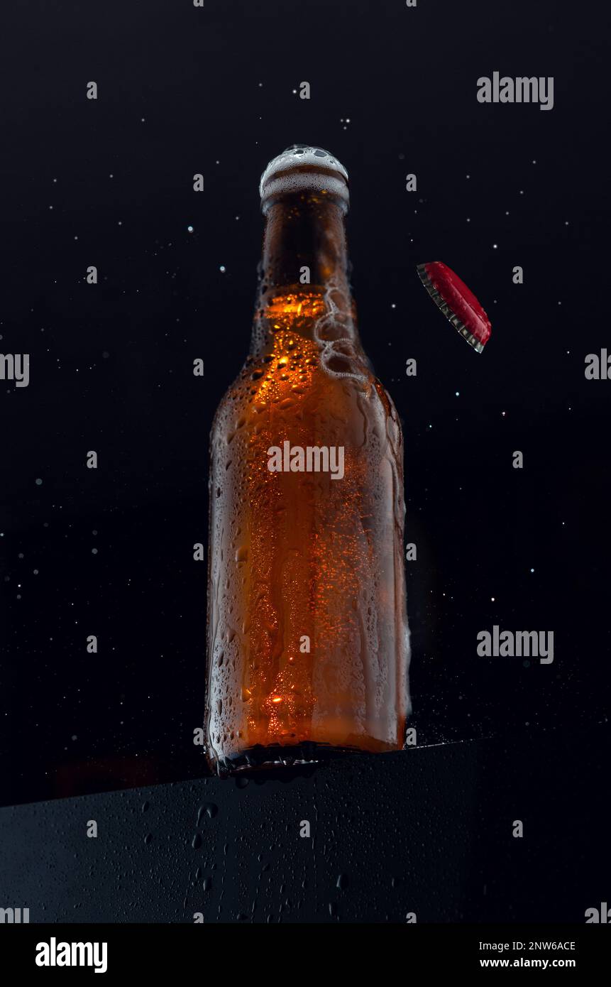 Cold beer bottle with the cap in the air seen from below on a black ...
