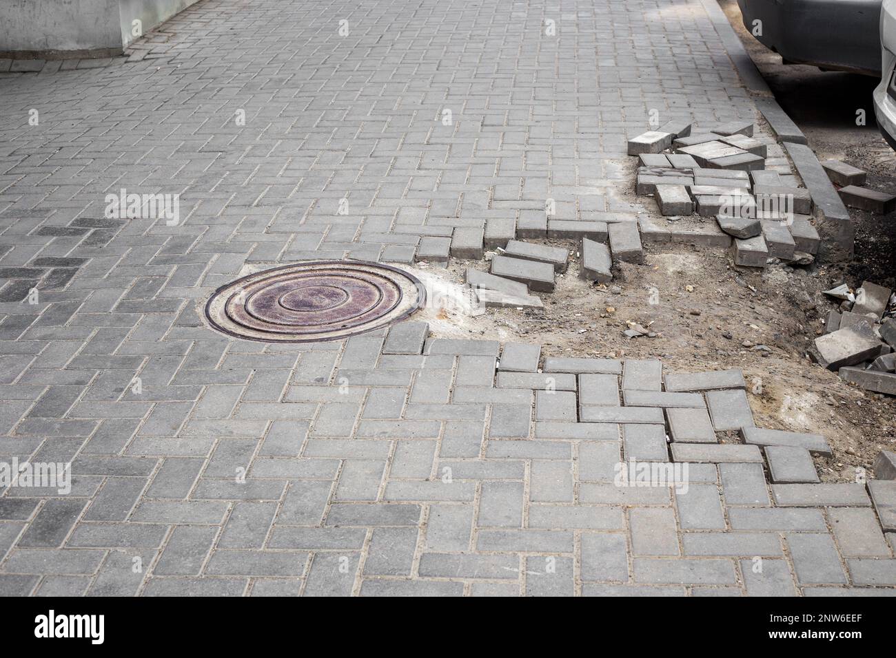 A city sidewalk with a well and crumbling paving stones. The problem of ...