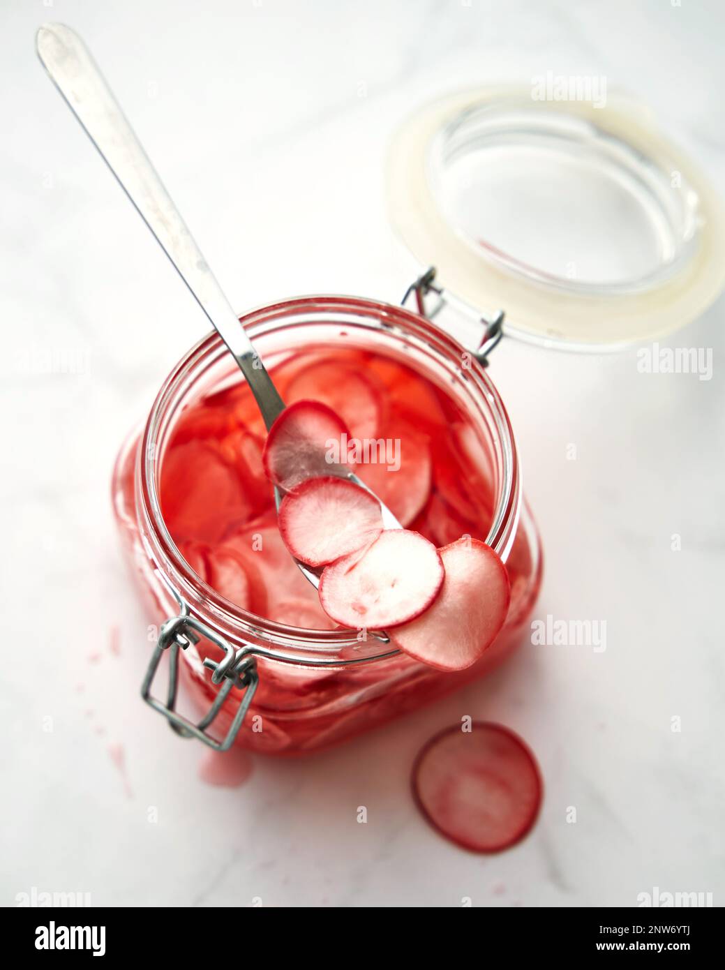 Jar of pickled thinly sliced pink radishes. A spoon is sticking out of ...