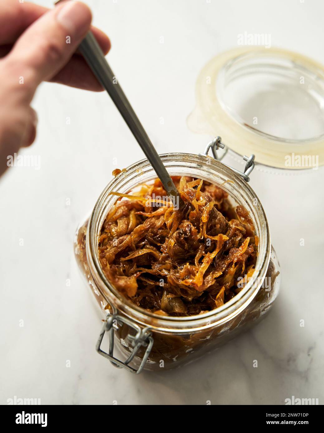 Homemade Caramelized onions in the jar. Man's Hand with spoon reaches ...