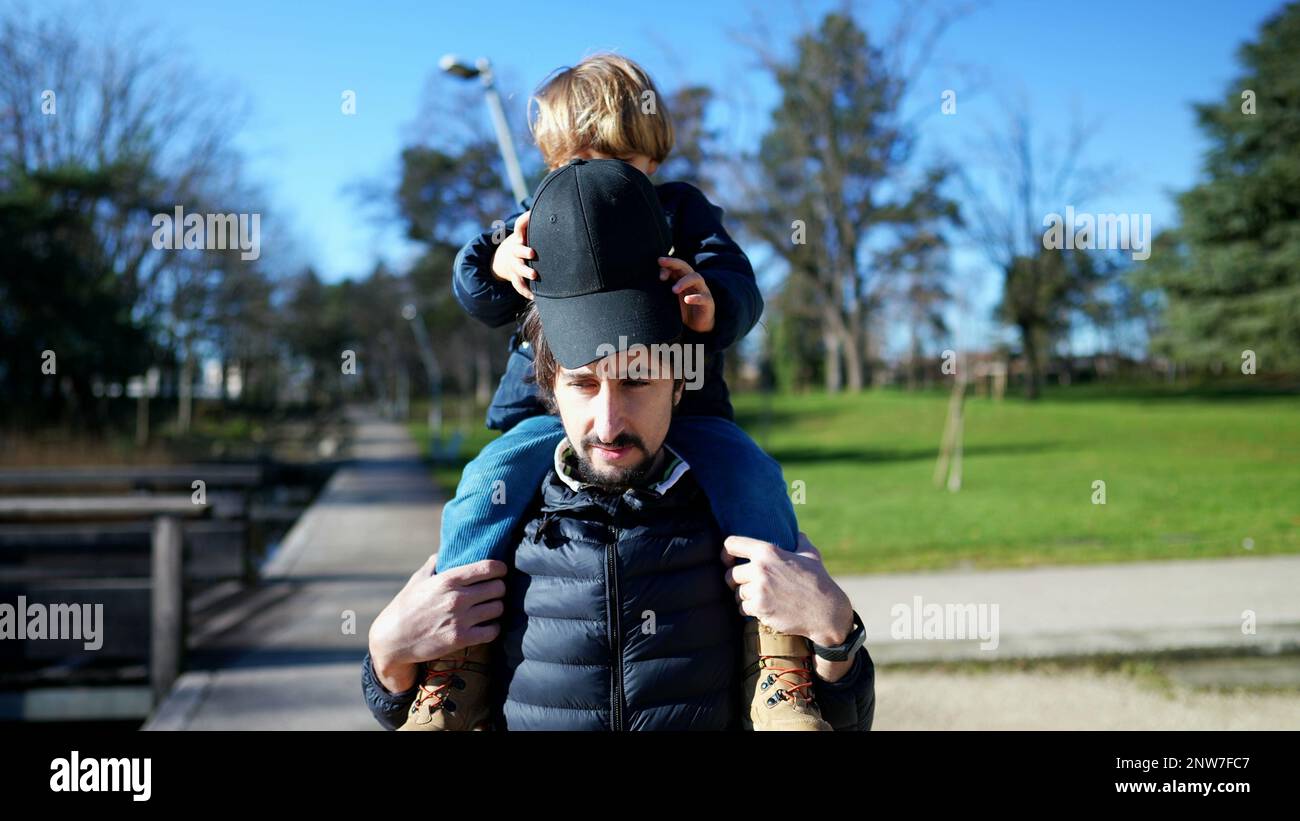 Little boy on father shoulder putting cap hat on dad head. Child and ...
