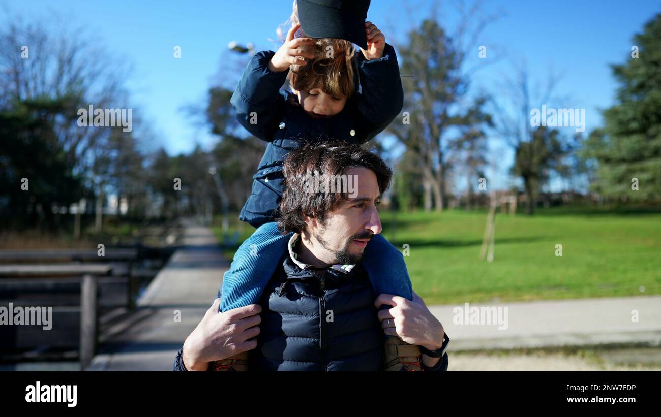 Little boy on father shoulder putting cap hat on dad head. Child and ...