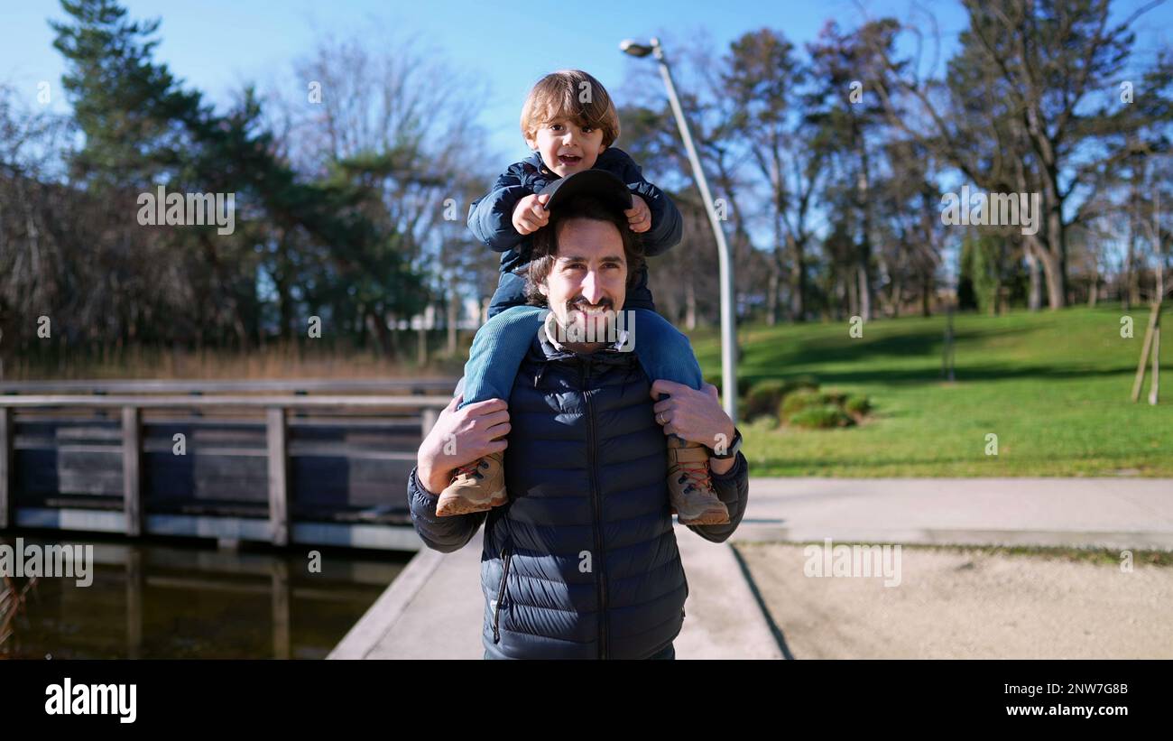 Little boy on father shoulders standing outside waving hello to camera ...