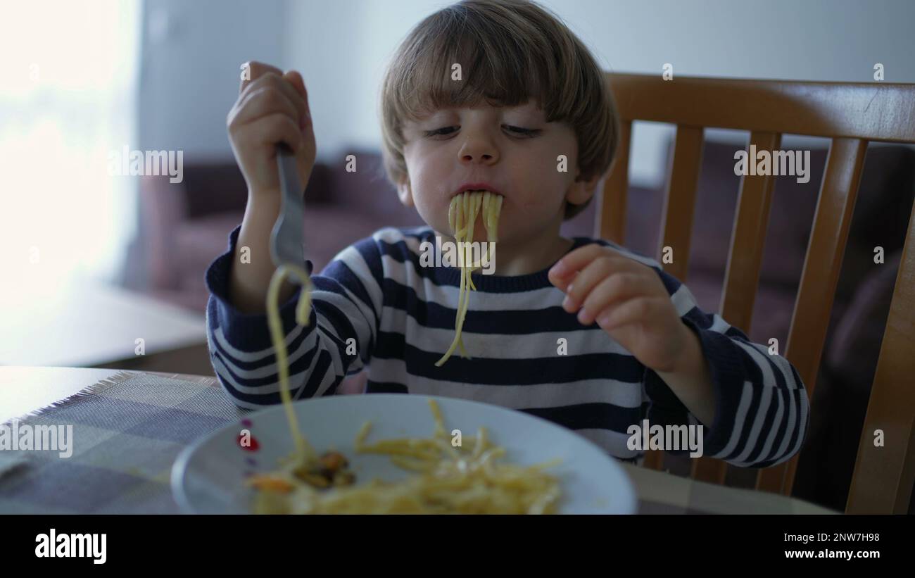 One cute little boy eating spaghetti meal. Child eats noodles by ...