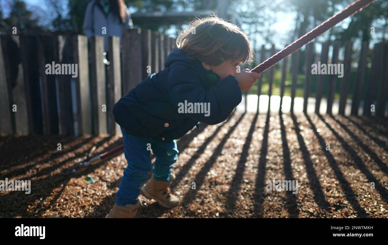 Small boy holding into playground rope during sunny winter season ...