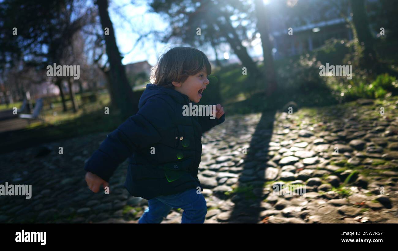 One happy small boy running outside in city park wearing jacket and ...