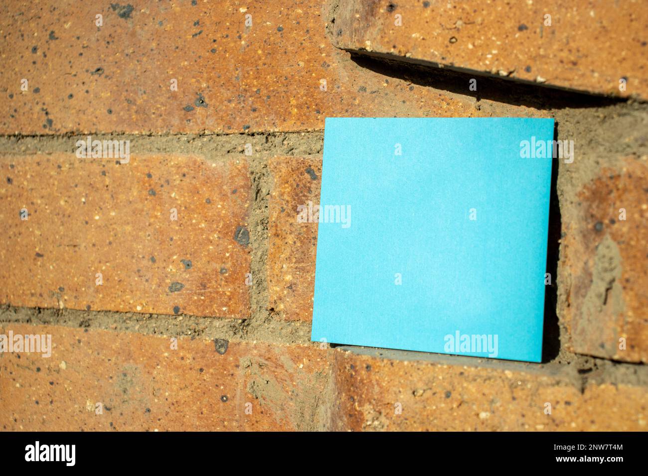 blue square paper note resting on a brick wall in full sun with empty ...