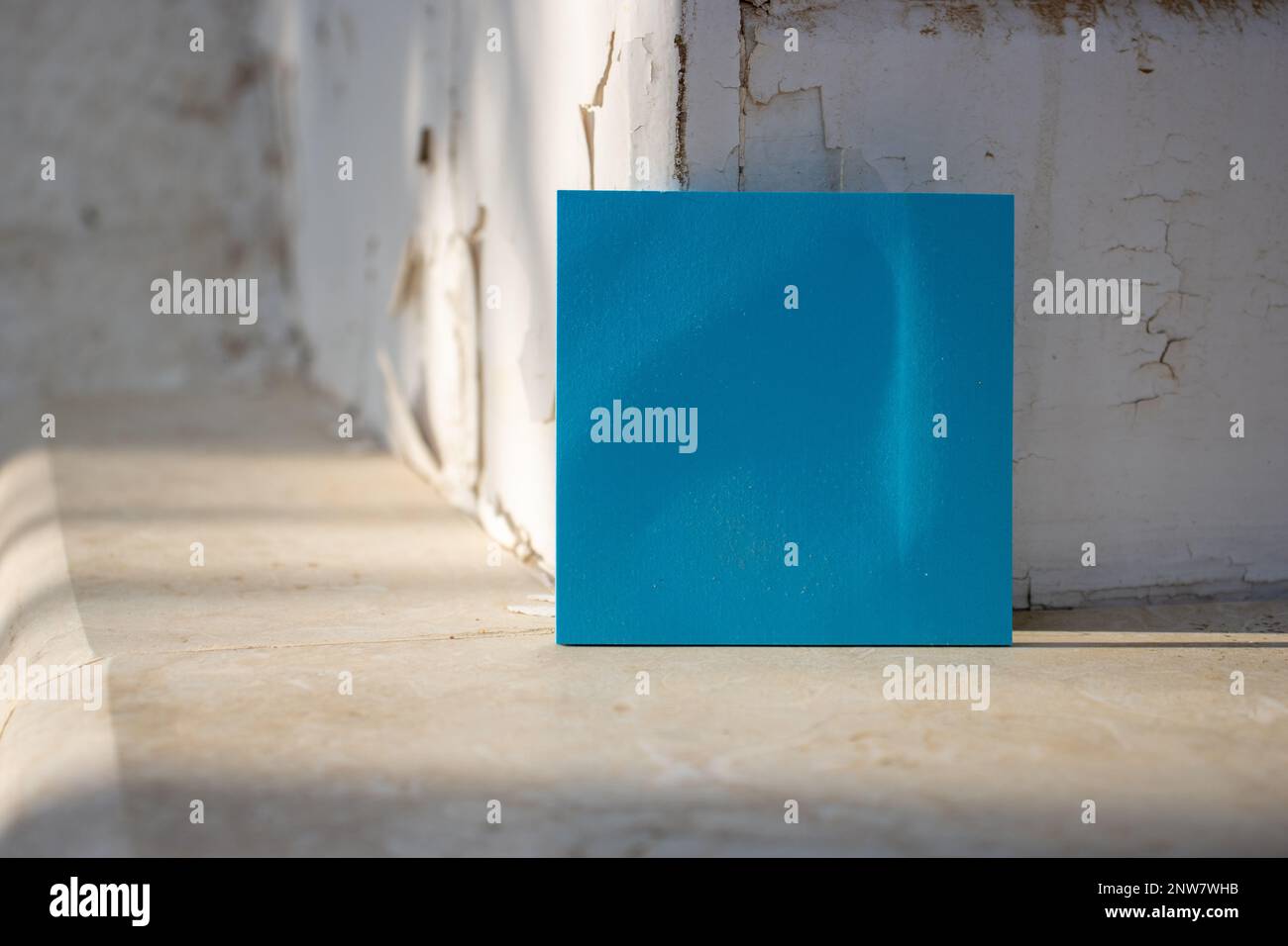 blue square paper note resting on old peeling white paint with empty ...