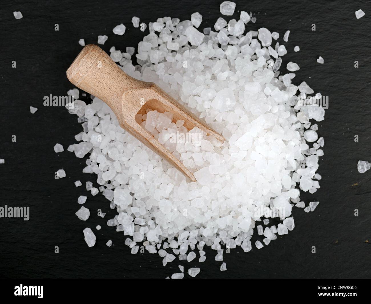 wooden spice scoop on heap of coarse sea salt on black slate stone, top ...