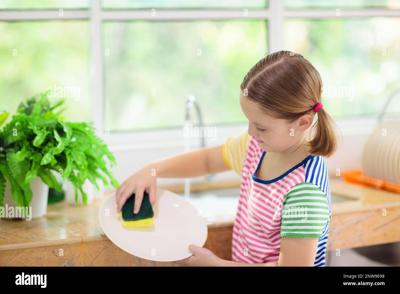 Child washing dishes. Home chores. Kid in white kitchen cleaning plates ...